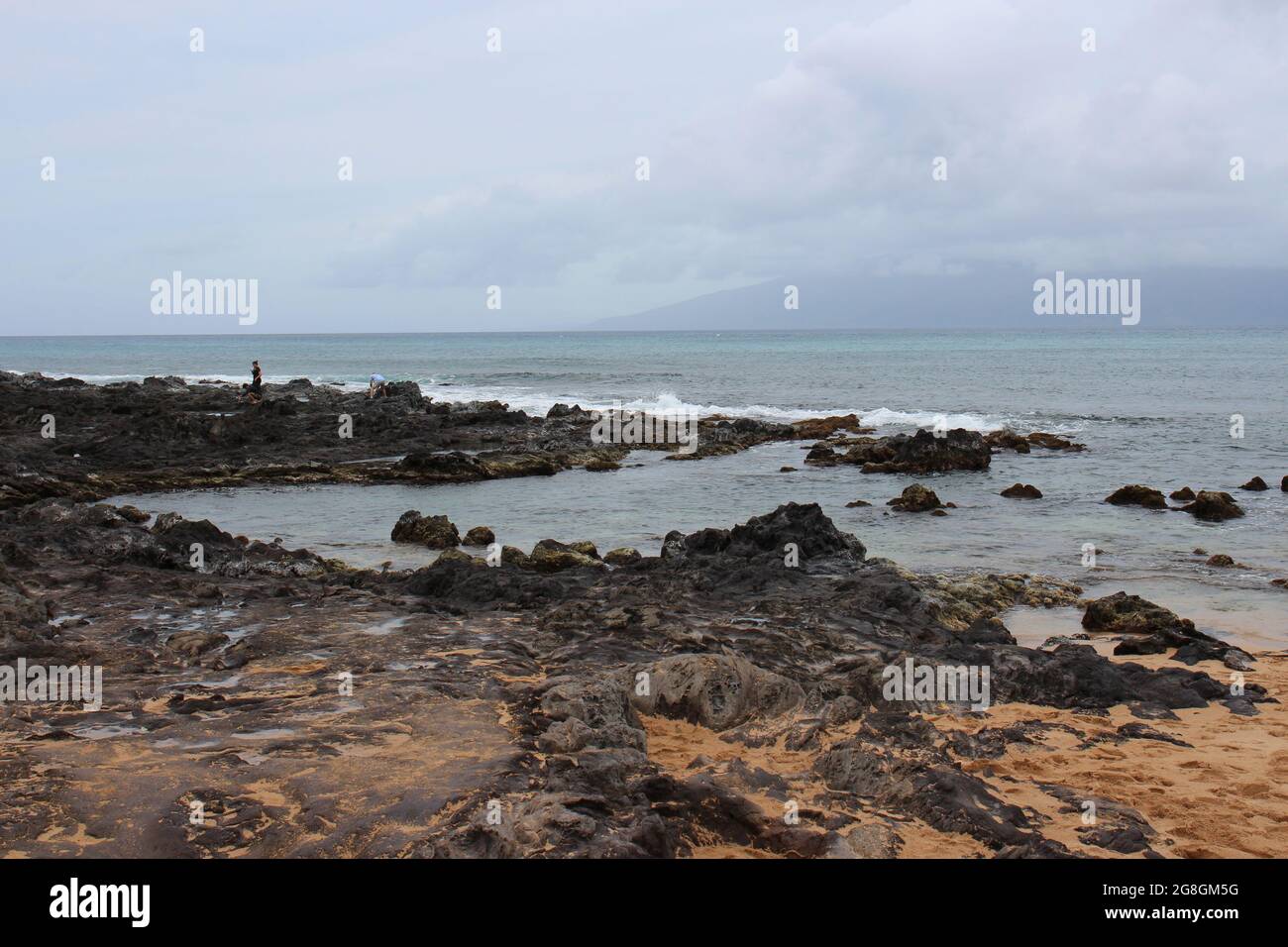 A volcanic rocky and sandy beach at low tide with tourists looking into ...