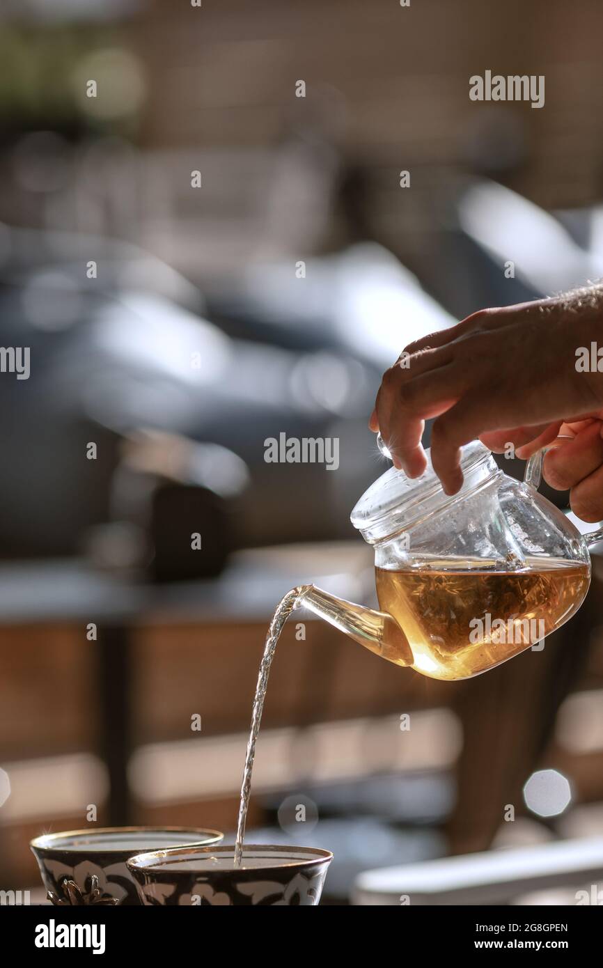Detail of male hands pouring fresh leaf herbal tea from clear glass ...