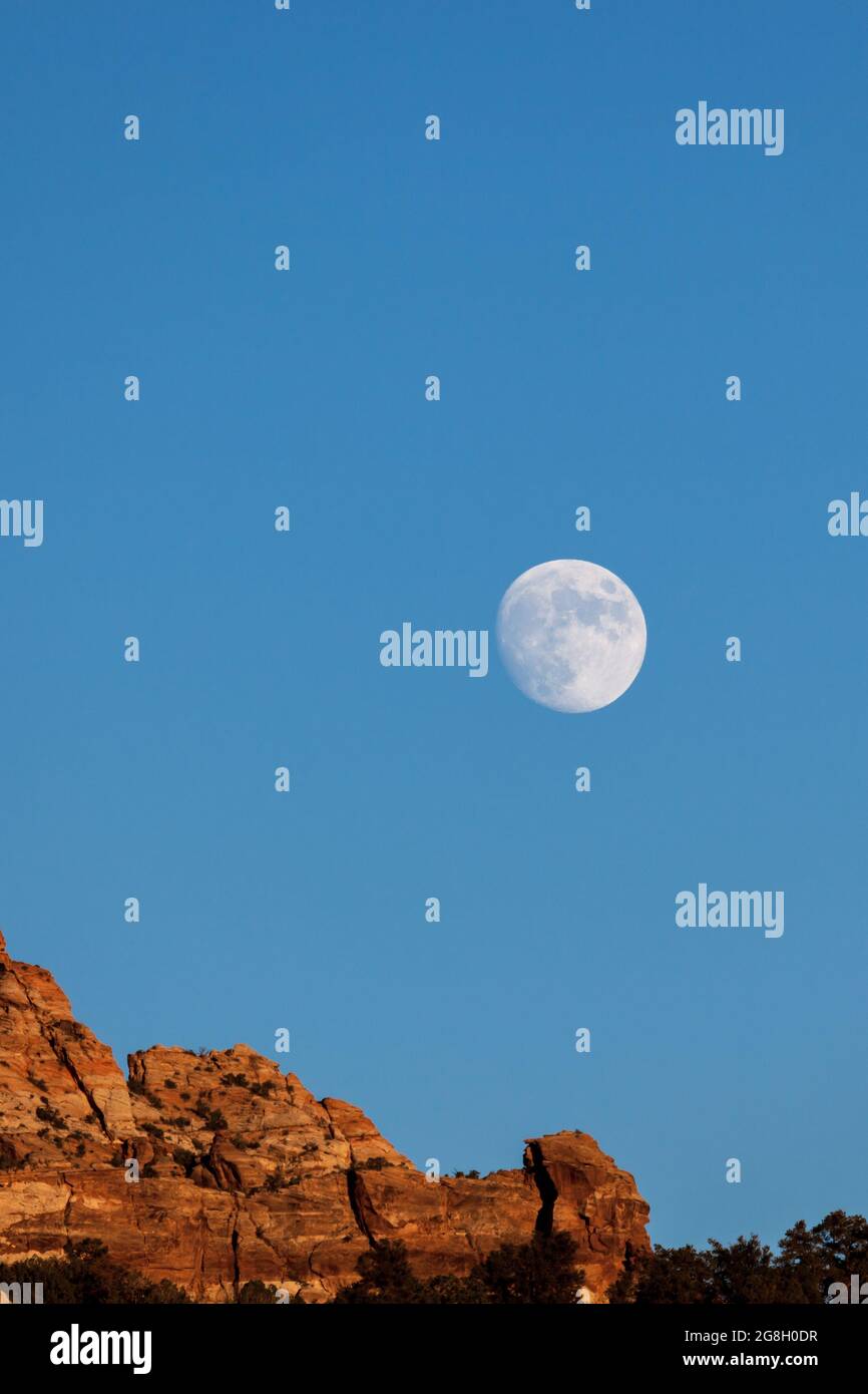 An almost full moon rising above red sandstone mountains with clear a ...