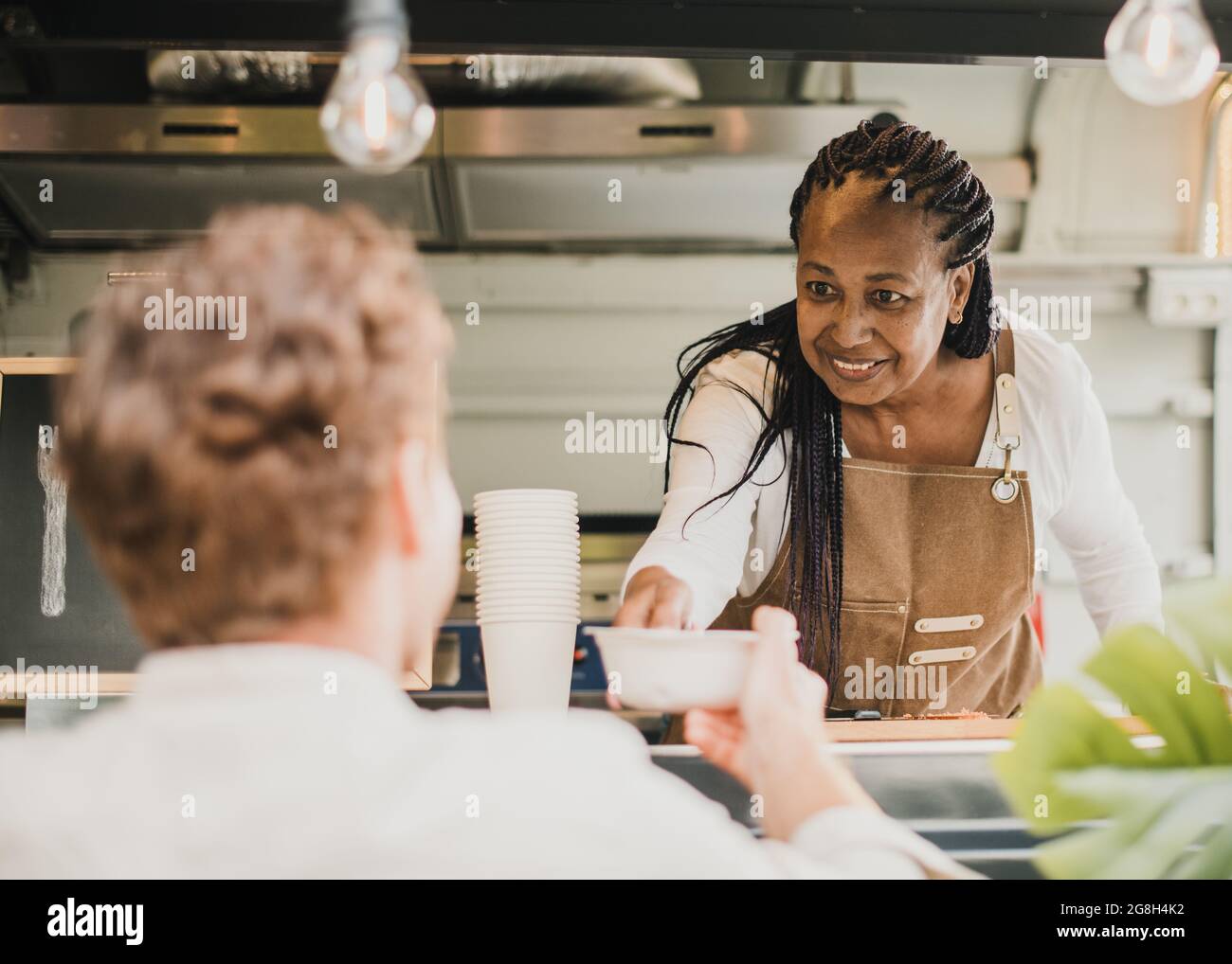 African chef woman serving take away order inside food truck - Focus on ...