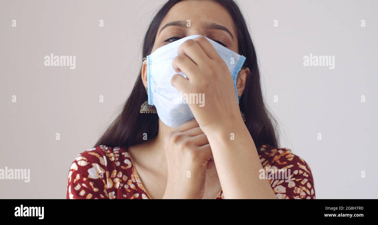Young Indian female fixing her face mask on background of a white wall ...