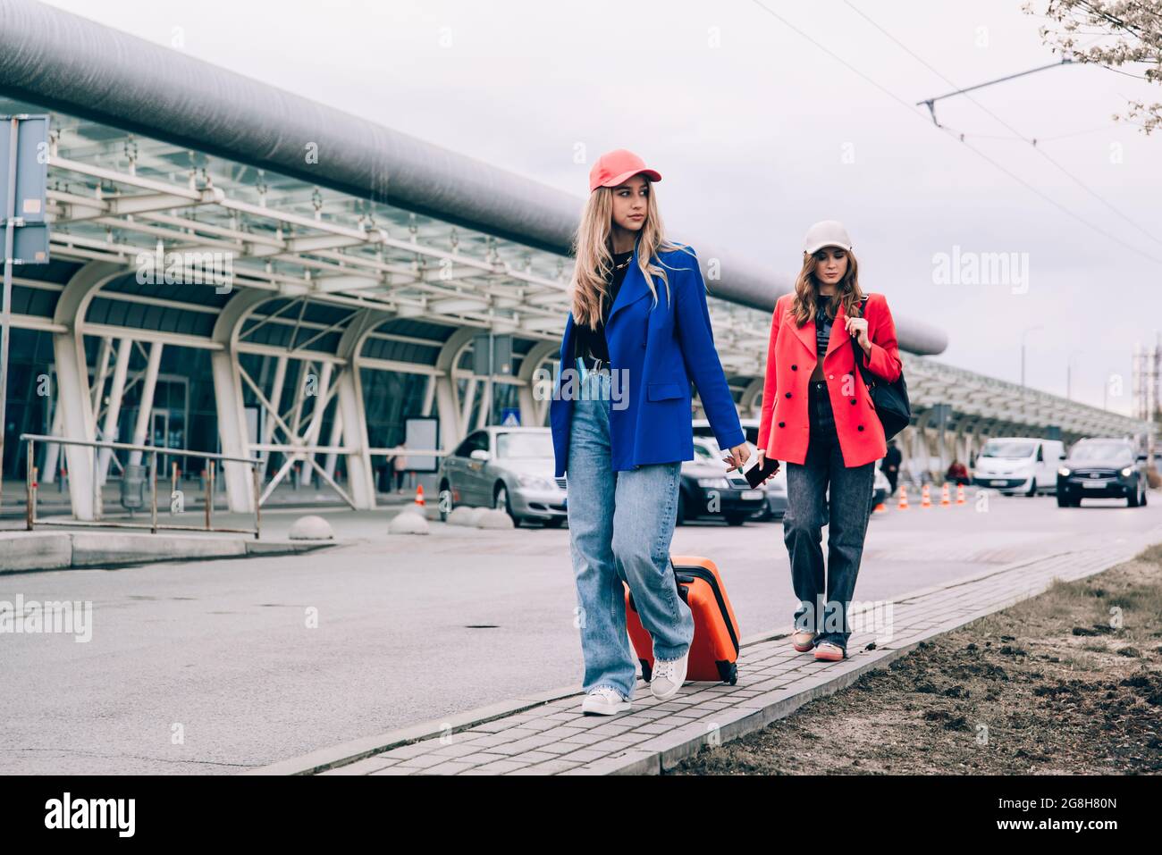Two happy girls walking near airport, with luggage. Air travel, summer ...