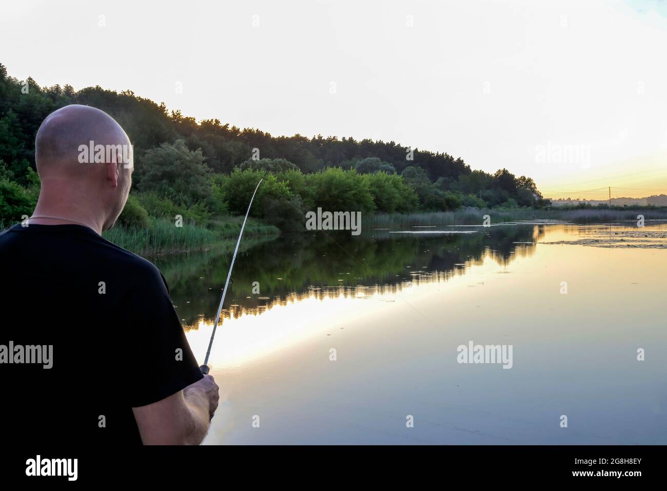 A man stands with his back and catches a fish with a fishing rod in the ...
