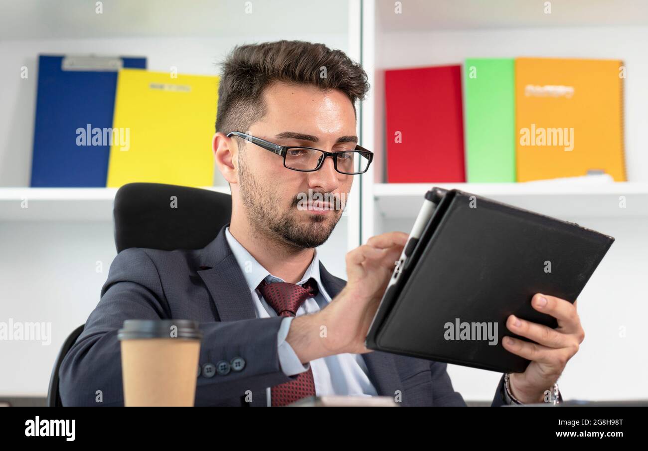 Cheerful young professional businessman in suit using digital tablet ...