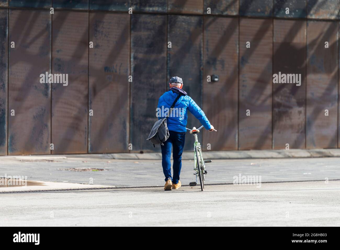 Senior man wheeling bicycle on city street holding a handbag Stock ...