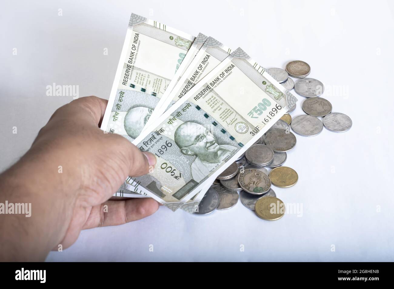 Hand holding Indian rupee bills with coins on a plain white table in ...