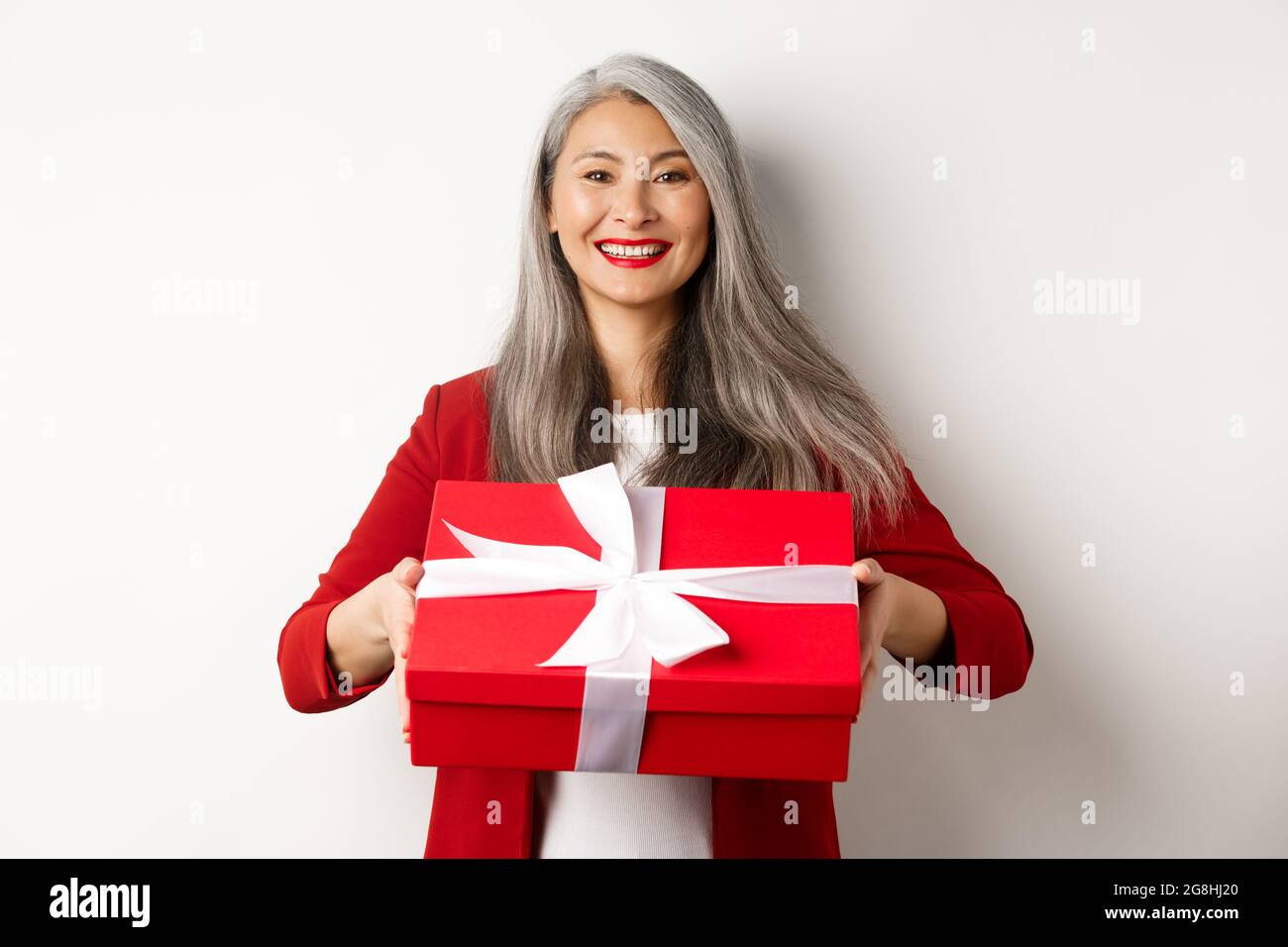 Elegant senior woman giving you present. Asian lady holding red gift ...