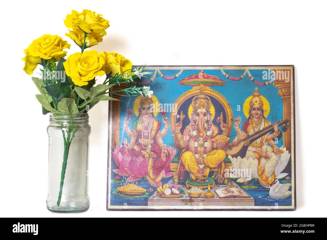 Jar of vibrant yellow roses next to a picture of the Hindu god Ganesha ...