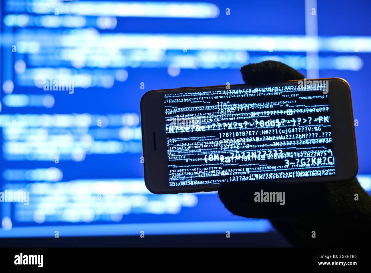 Hacker with mobile phone near screen of computer Stock Photo - Alamy