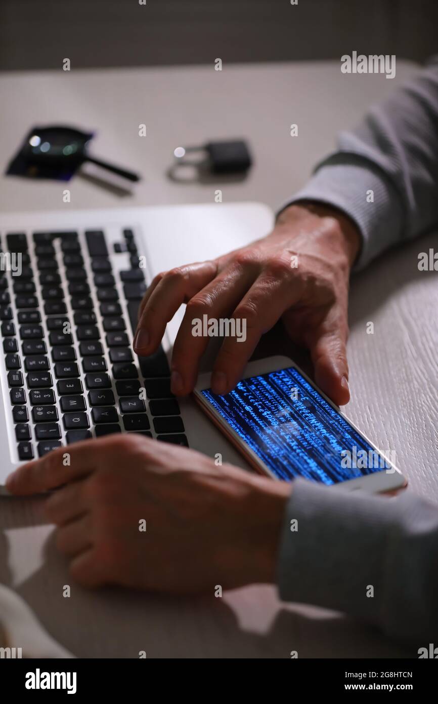 Hacker with mobile phone using computer in dark room Stock Photo - Alamy