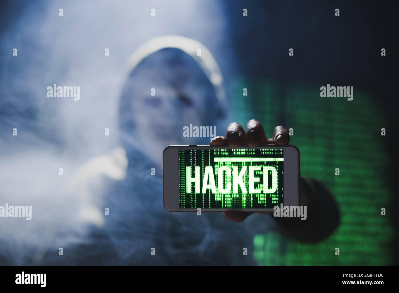 Hacker holding mobile phone with word HACKED on screen against dark ...