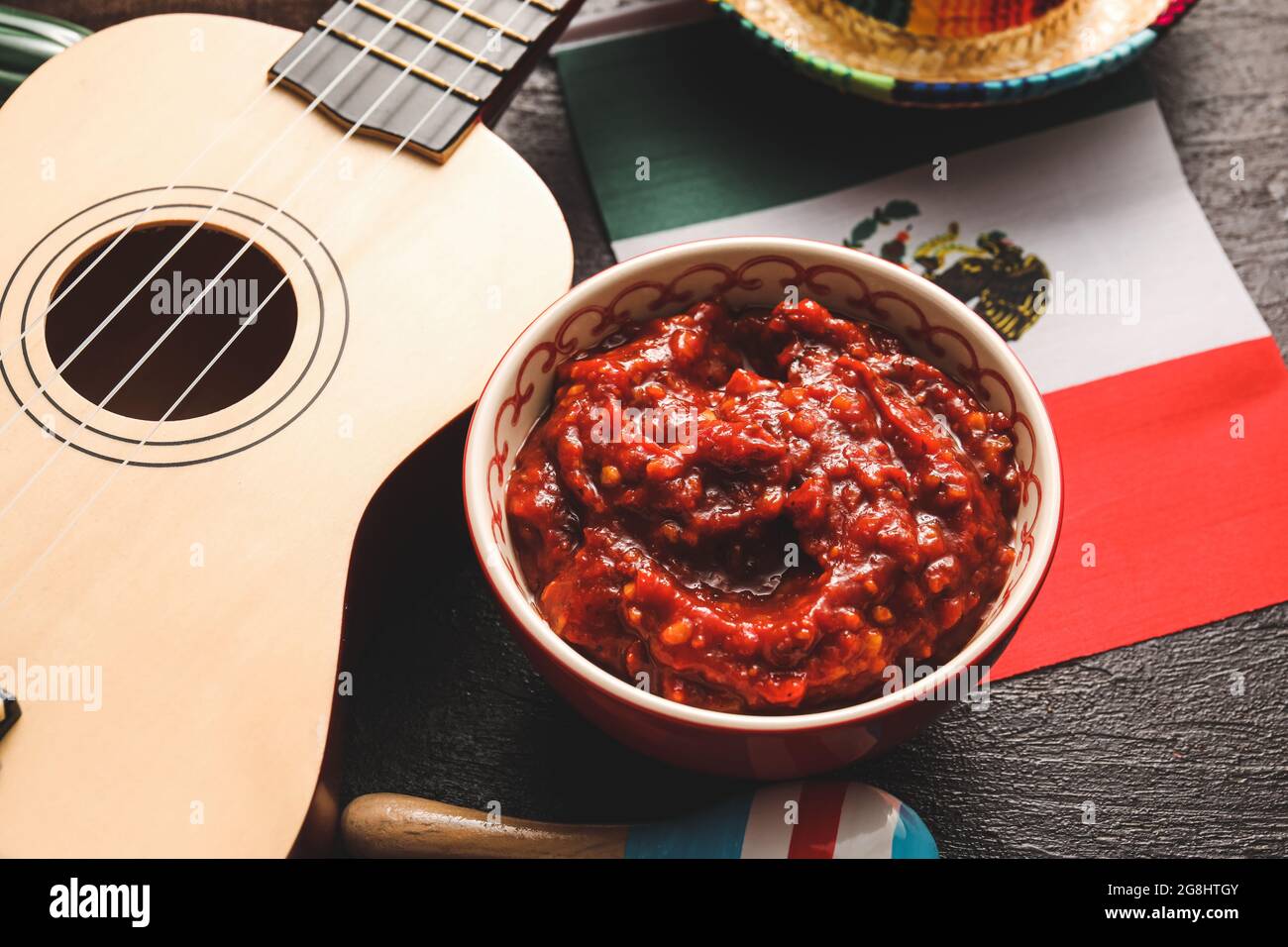 Bowl of tasty salsa sauce with symbols of Mexico on dark background ...