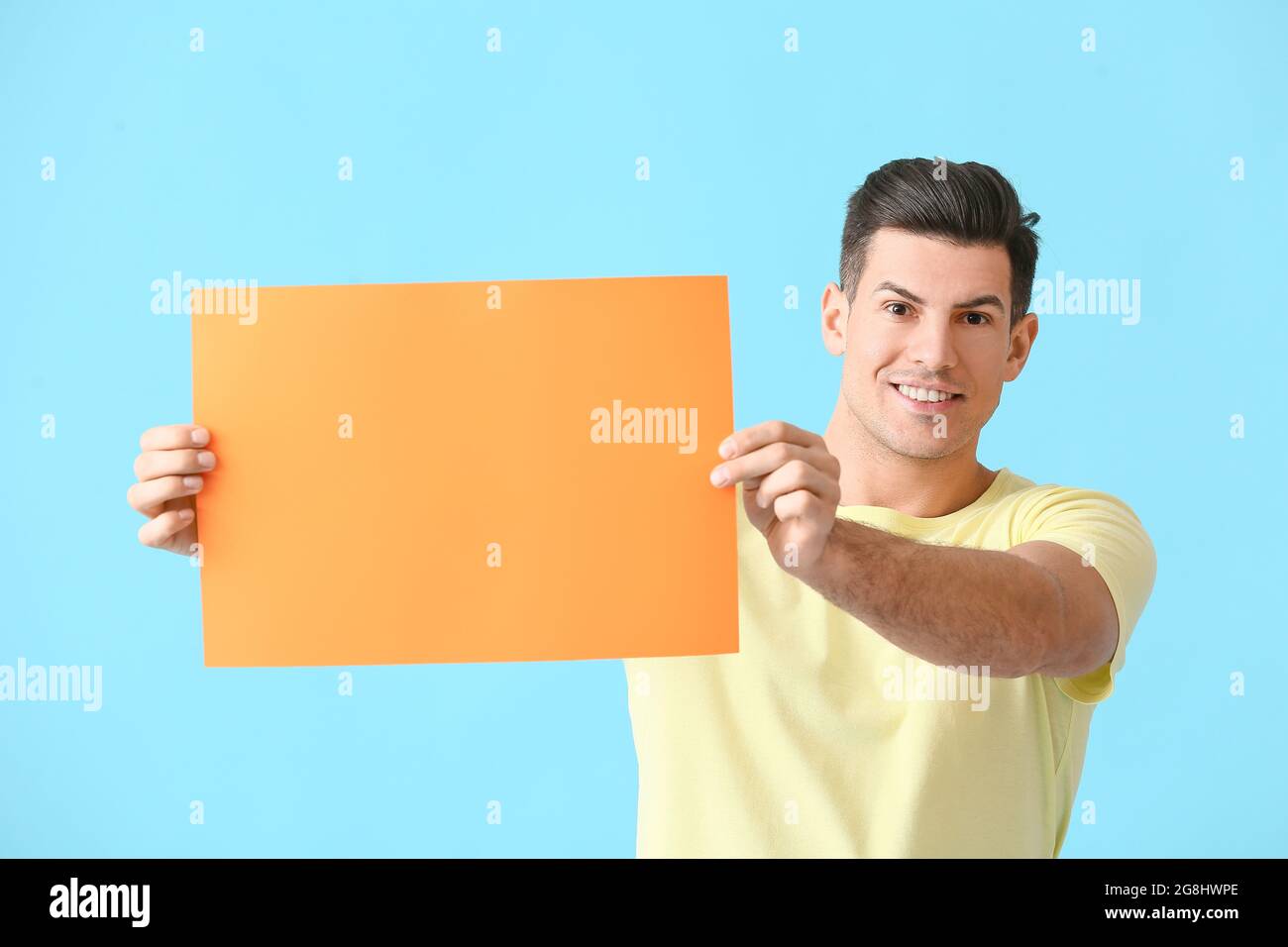 Young man with blank paper sheet on color background Stock Photo - Alamy