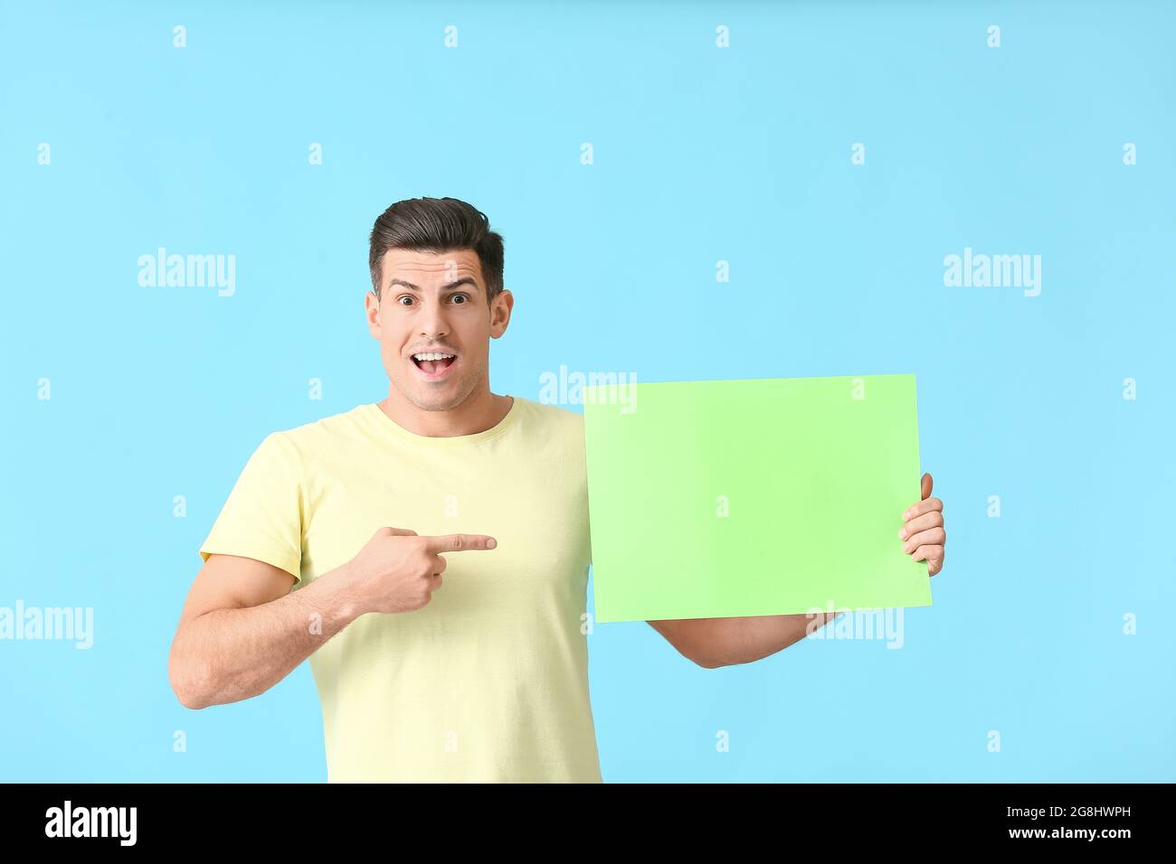 Surprised young man pointing at blank paper sheet on color background ...