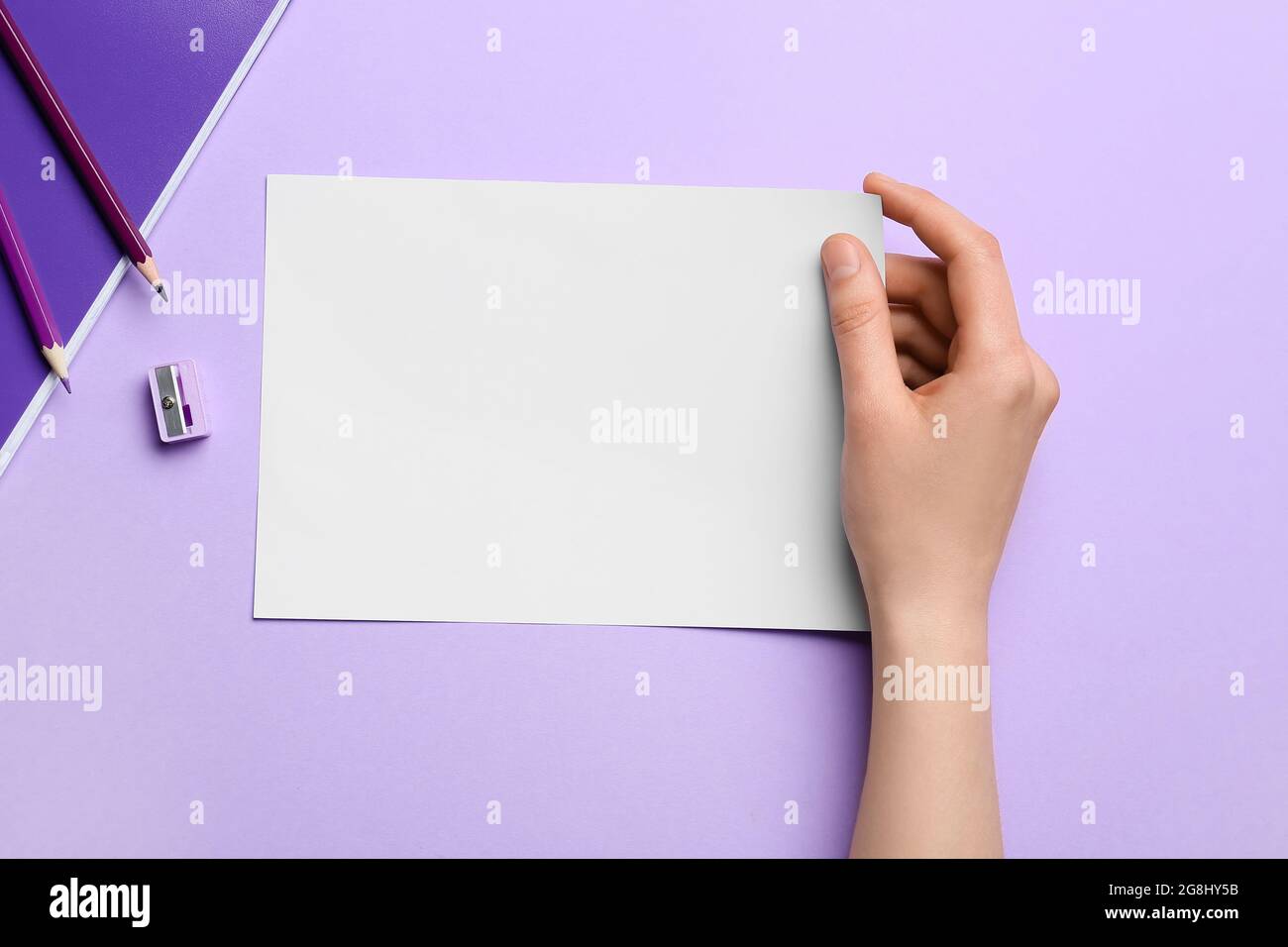 Female hand with blank sheet of paper, pencils and sharpener on color ...