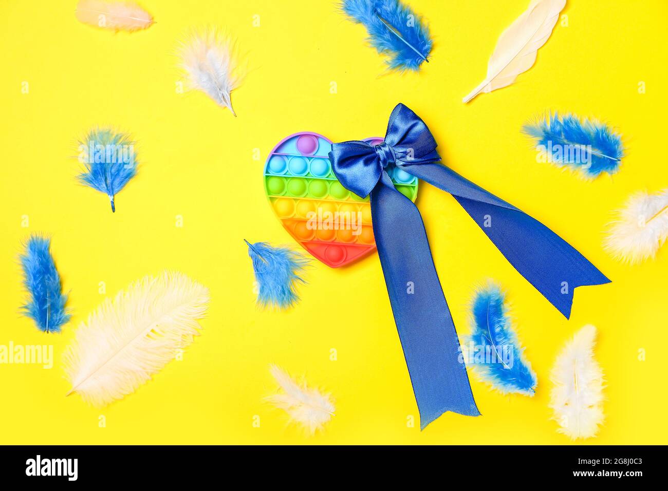 Pop it fidget toy and feathers on color background Stock Photo - Alamy