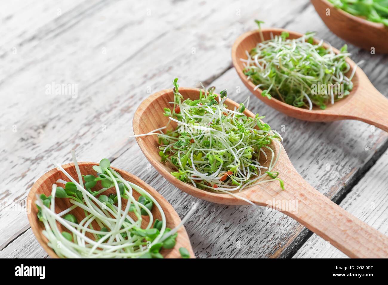 Spoons with different fresh micro green on light wooden background ...