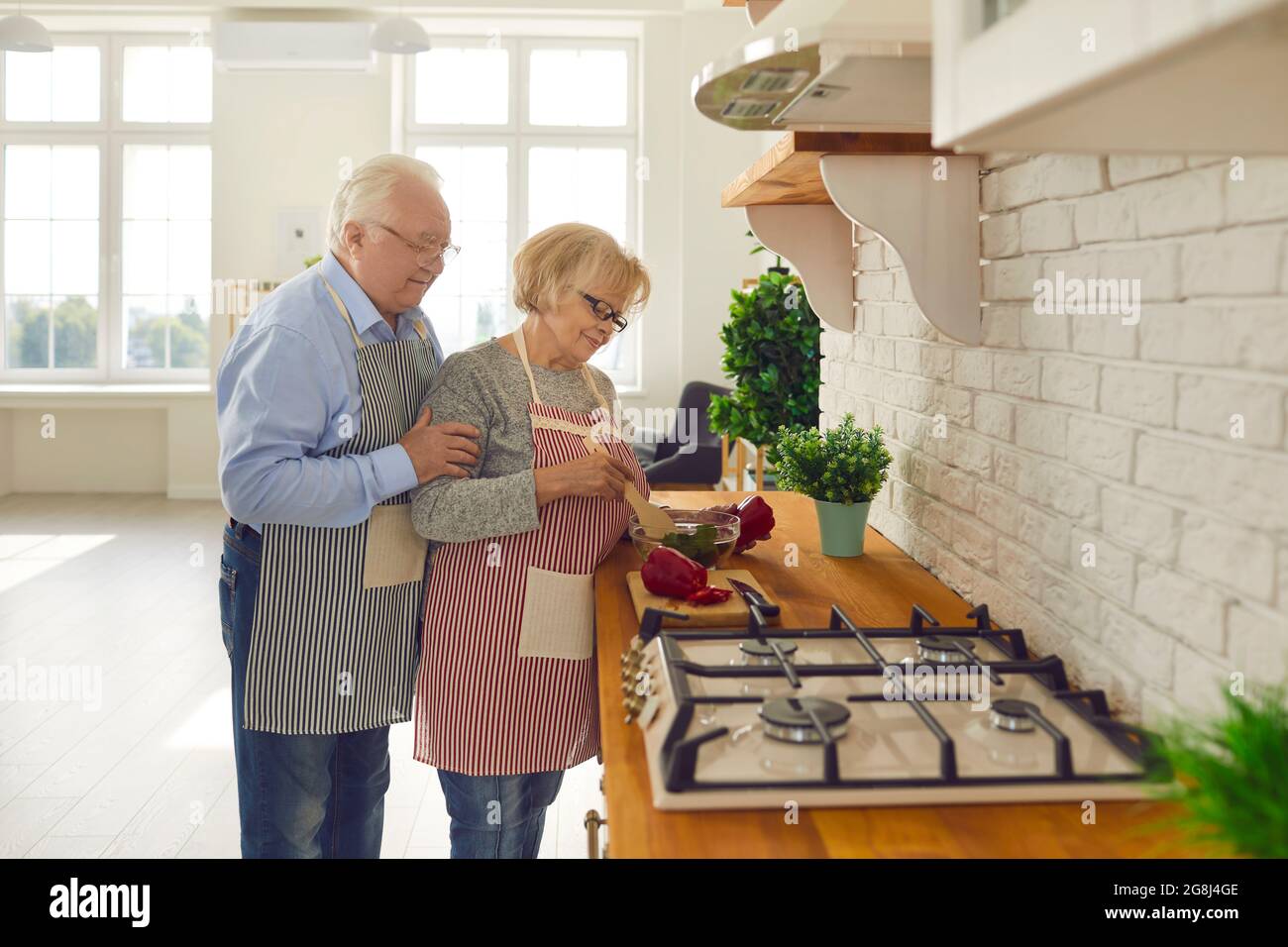 Happy loving senior husband helping his wife to make healthy vegetarian ...
