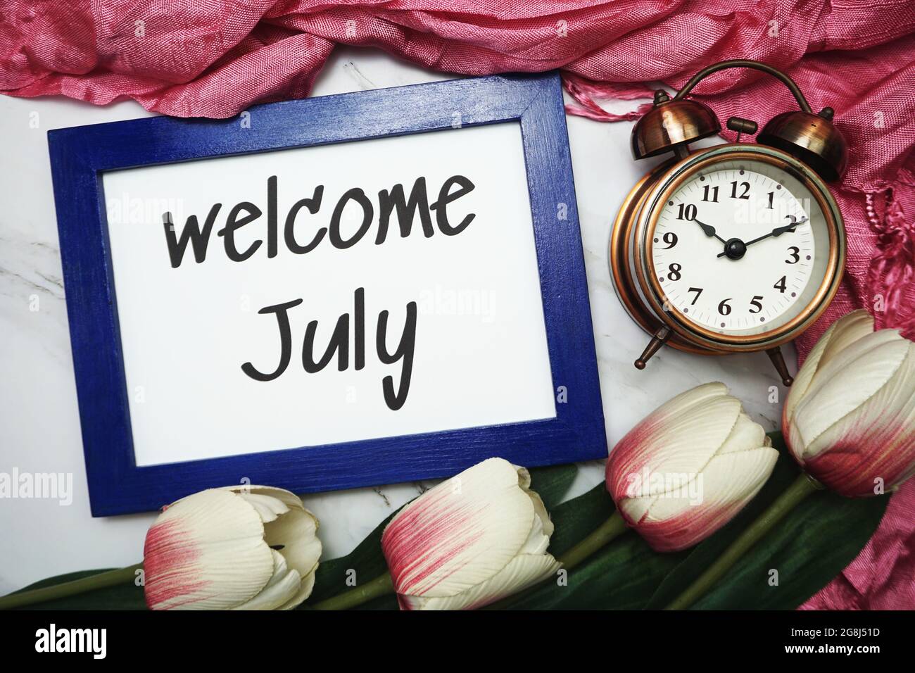 Welcome July written on blue frame with tulip flower flat lay on marble ...