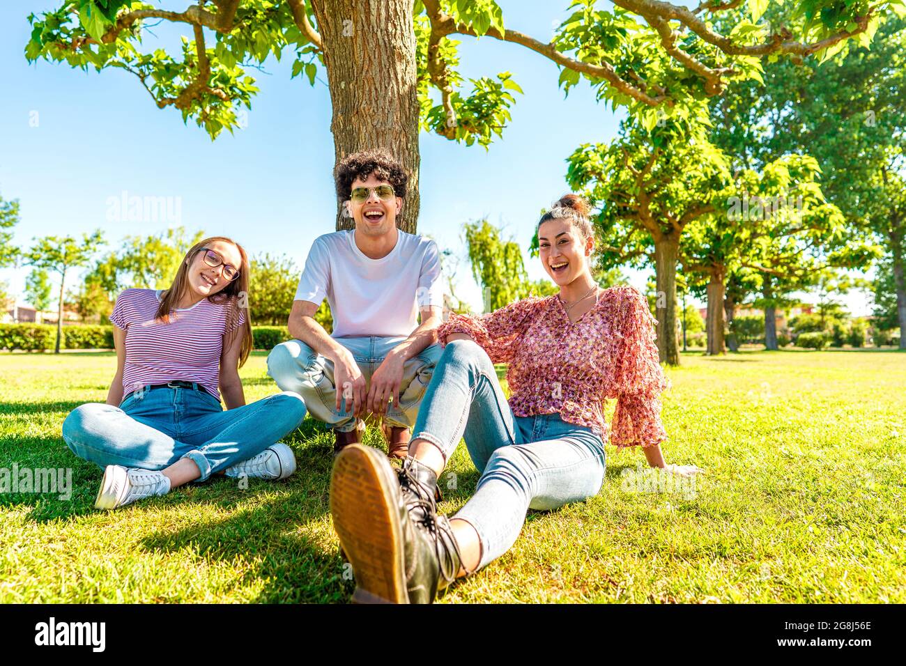 Three young diverse friends resting on green park field smiling looking ...