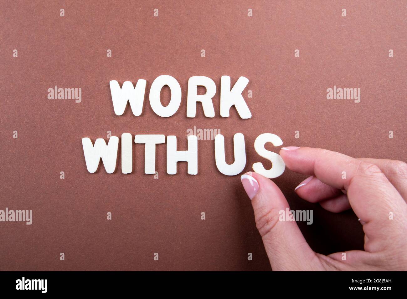 Work With Us. White letters and a woman's hand on a brown background ...