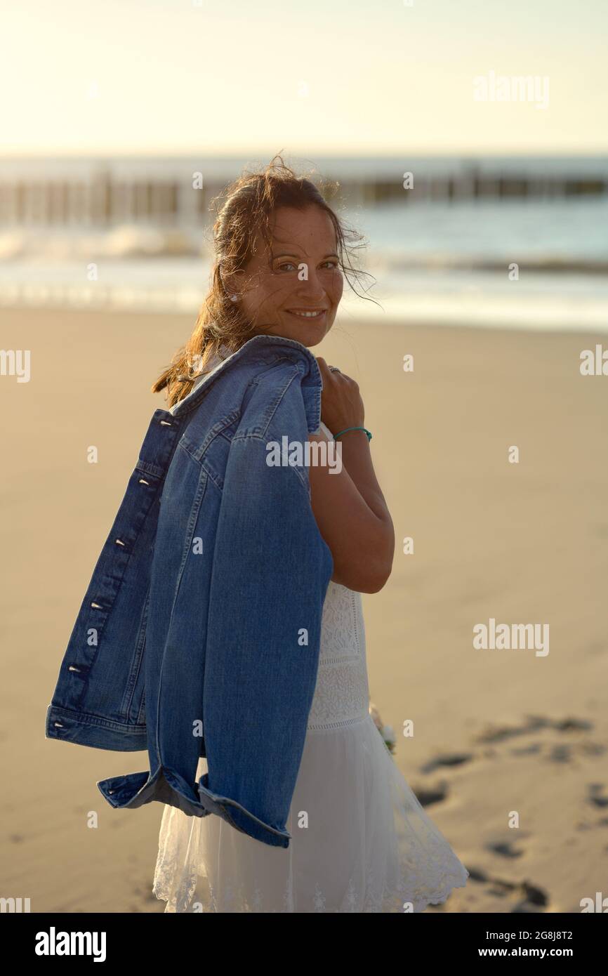 Attractive middle-aged woman in stylish white dress carrying a bouquet ...