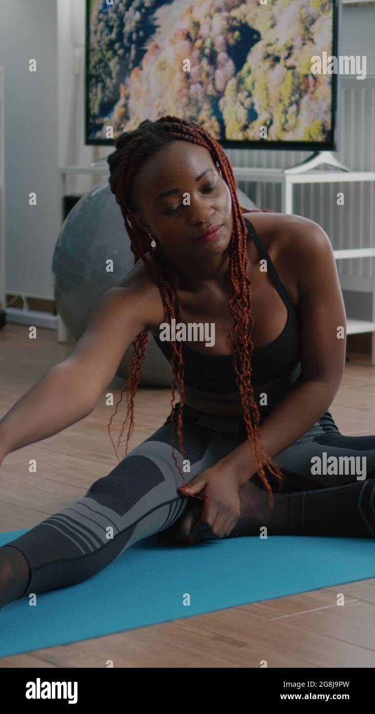 Flexible fit black woman doing stretching routine on yoga map in living ...
