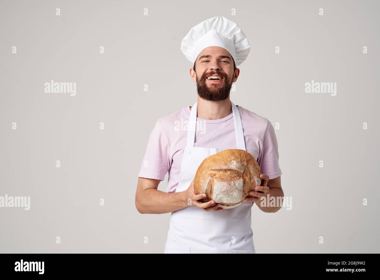 bearded man in a white apron with bread in his hands baking light ...