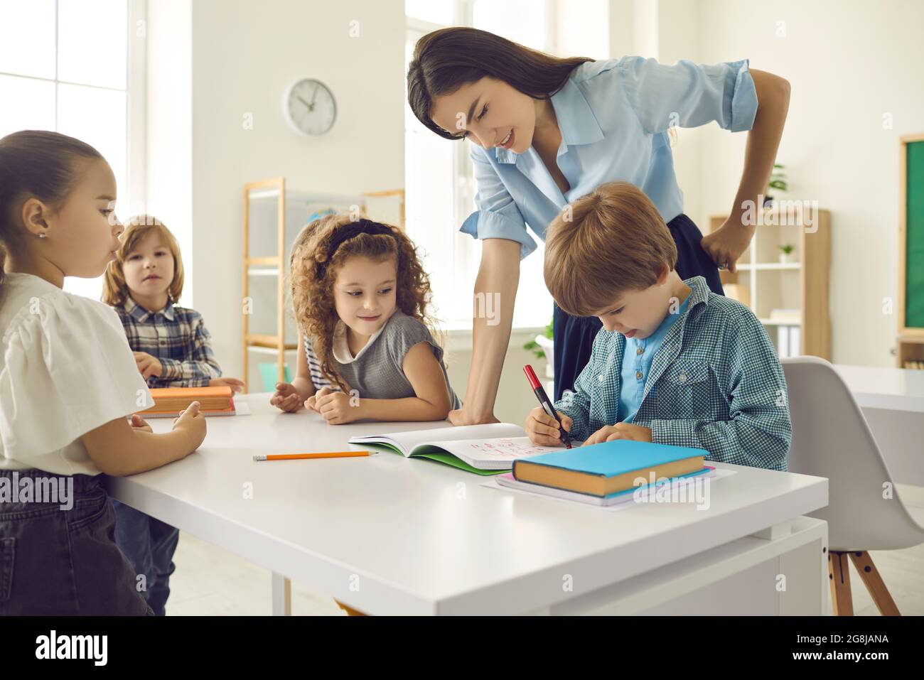 Young school teacher helping her little students who are writing in ...