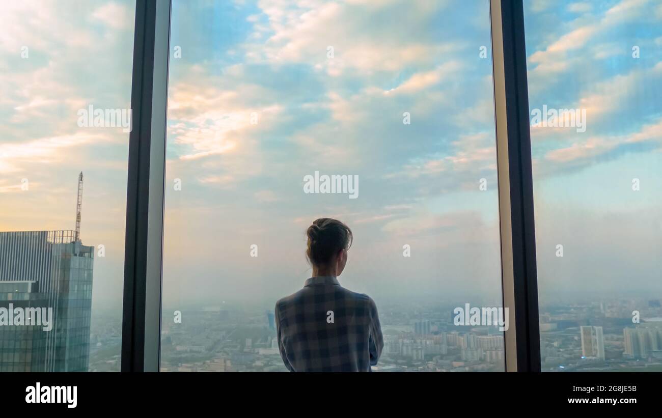 Back view of pensive woman looking at cityscape through window of ...