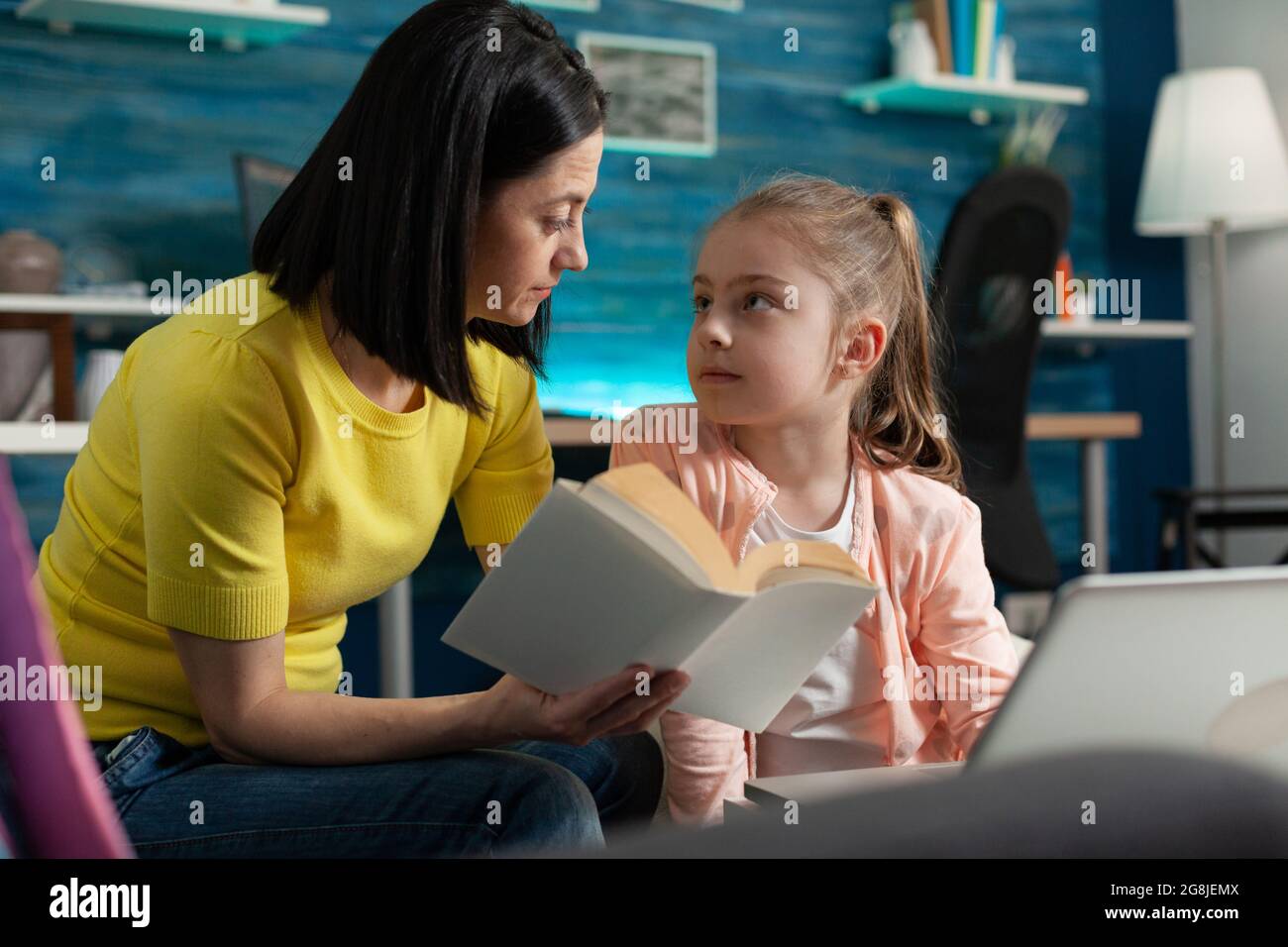 Mother assisting little child on reading school book while sitting at ...