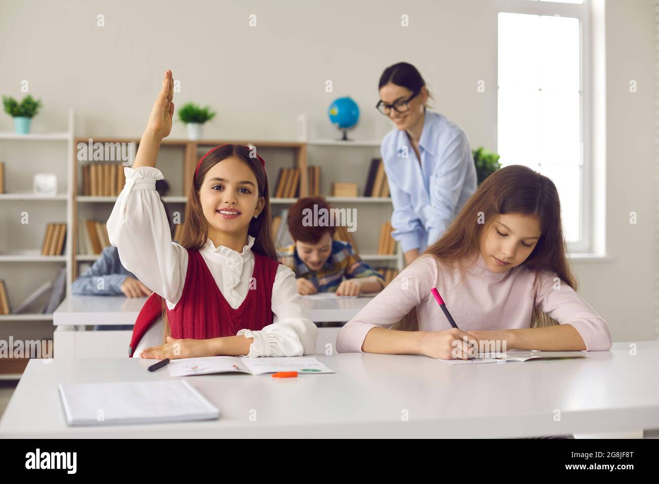 Happy primary school student raising hand to answer teacher's questions ...