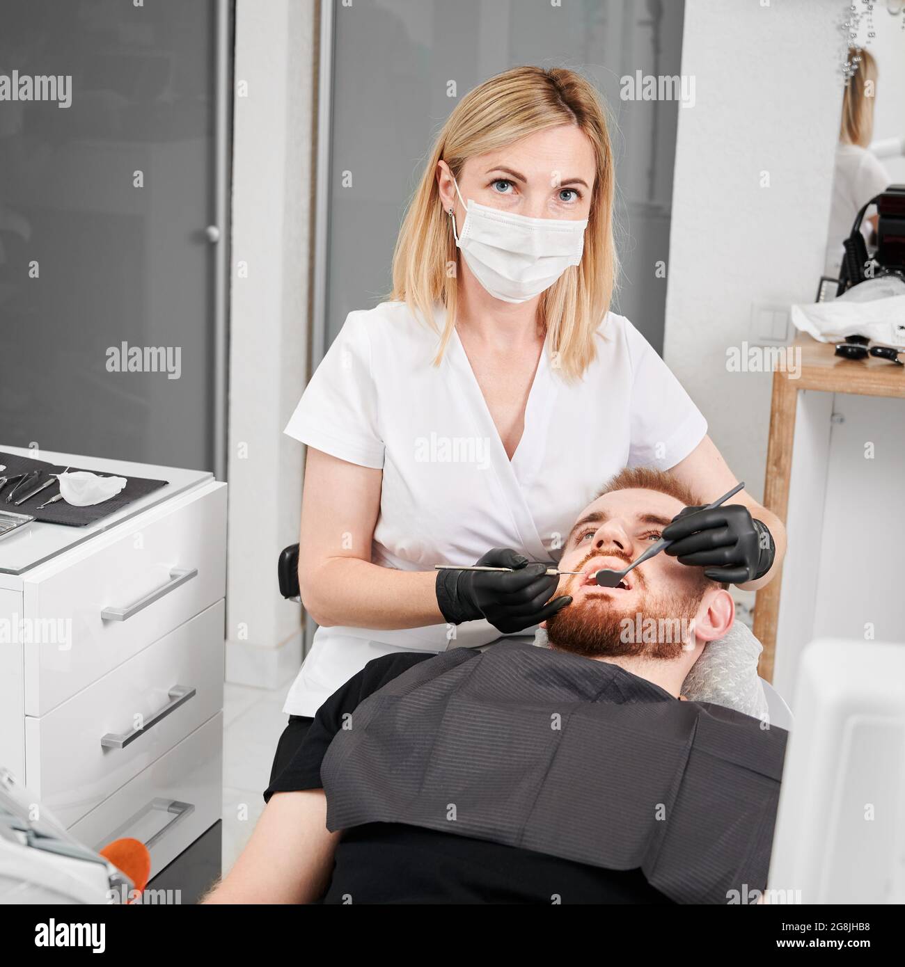 Woman stomatologist in medical mask looking at camera while examining ...