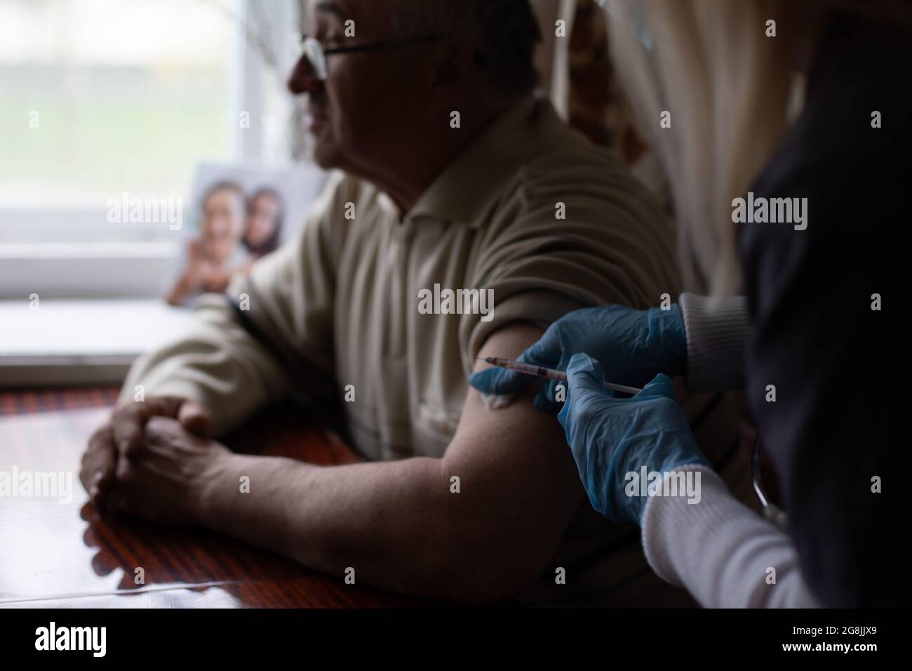 Young woman doctor injecting vaccine to elderly man during home visit ...