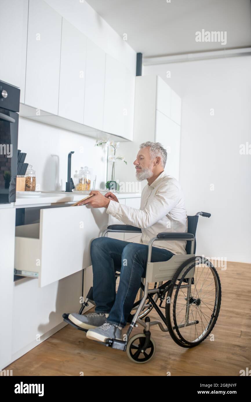 Gray-haired handicapped man in the kitchen getting the breakfast ready ...