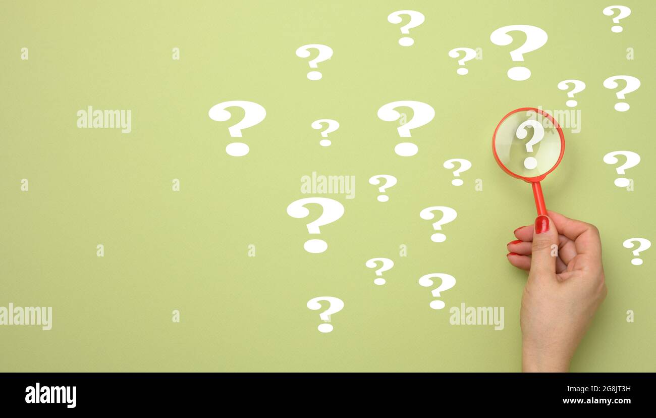 female hand holds a plastic magnifying glass and question marks on a ...