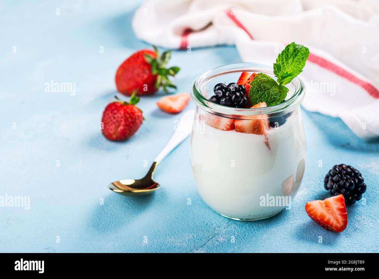 Two portions of greek yogurt with summer berries in glass jars on blue ...