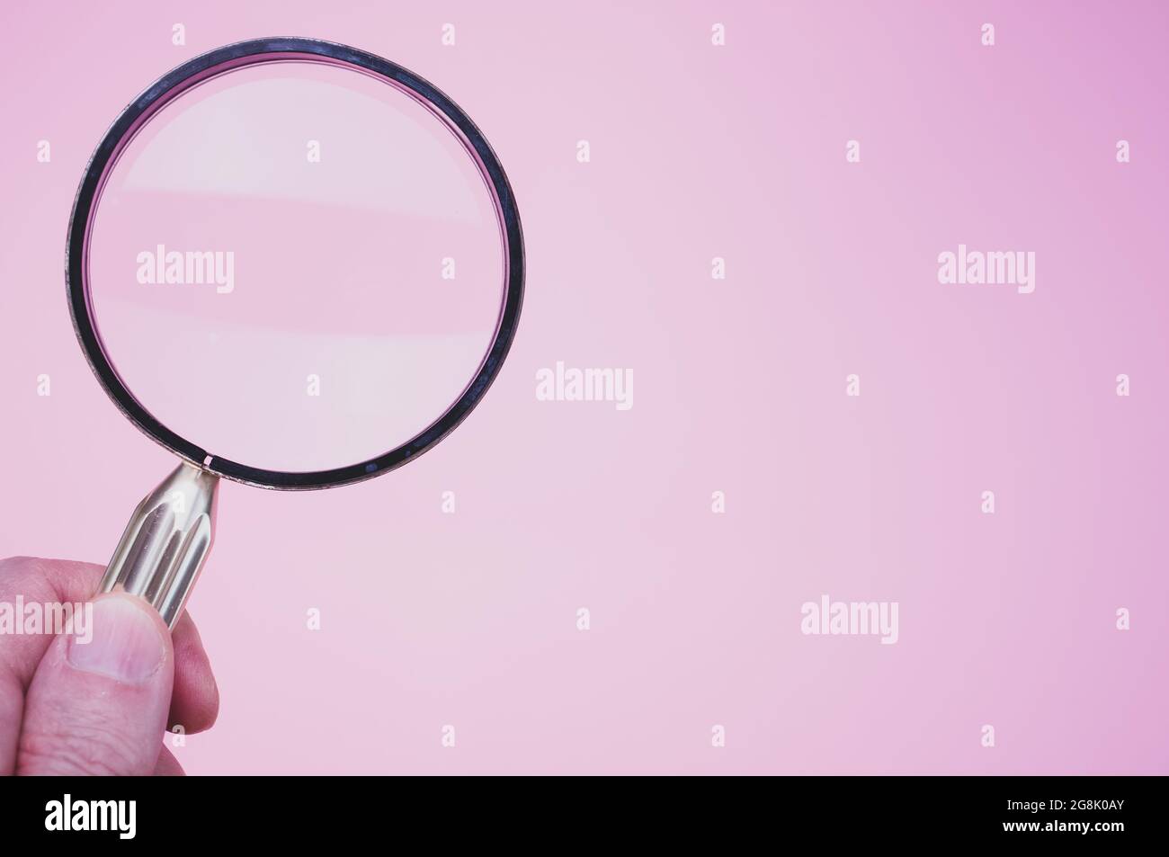 Hand holding a magnifying glass on a pink background Stock Photo - Alamy