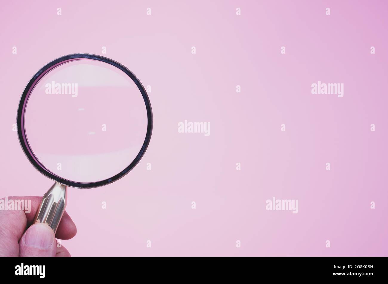 Hand holding a magnifying glass on a pink background Stock Photo - Alamy