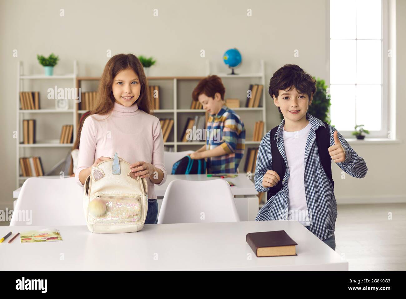 Elementary school children standing at classroom desk gesturing thumbs ...