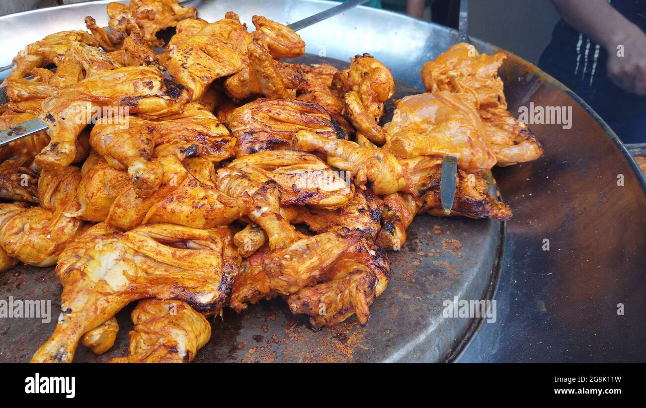 Closeup of Indian Tandoori chicken being cooked on a big silver stove ...