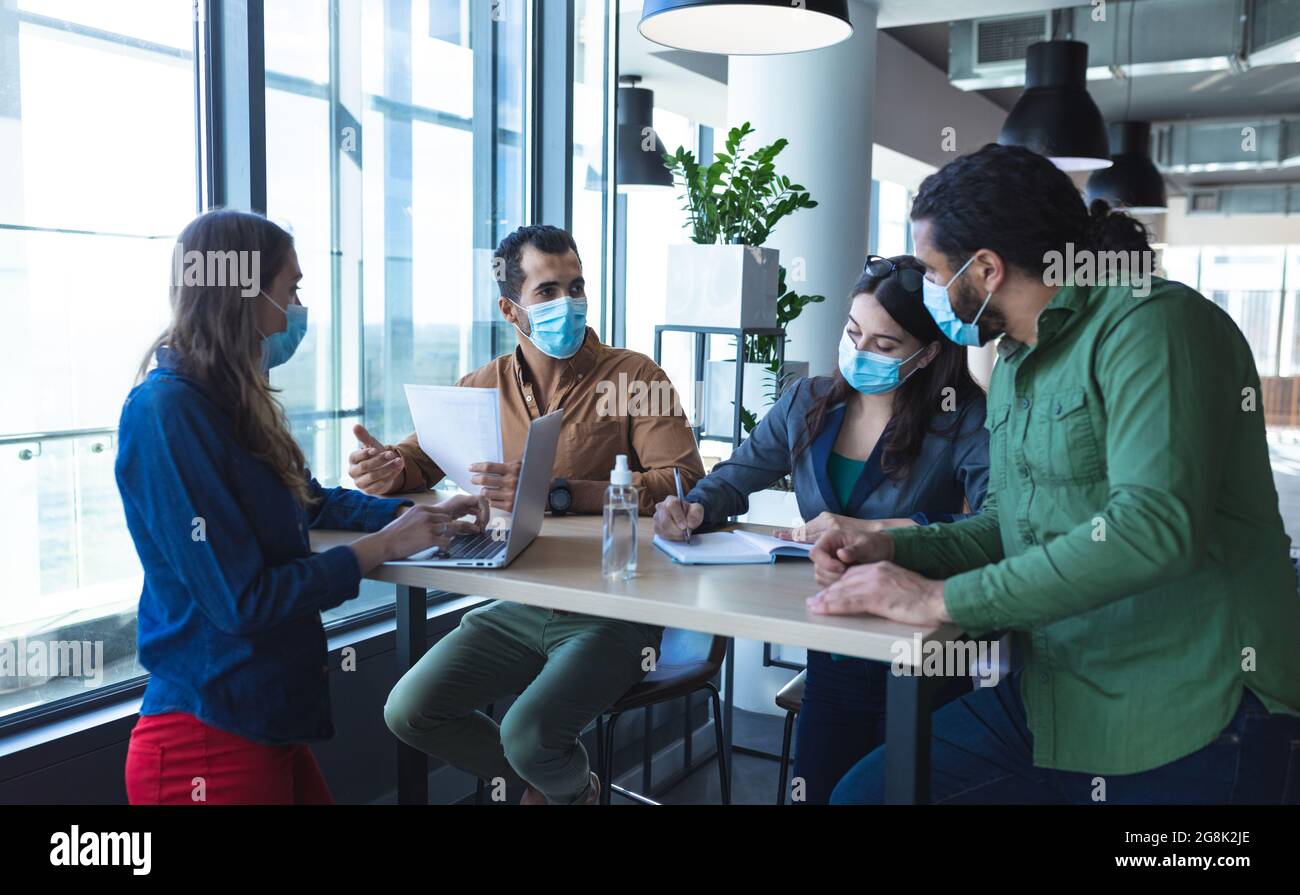 Diverse group of creative colleagues wearing face masks talking at ...