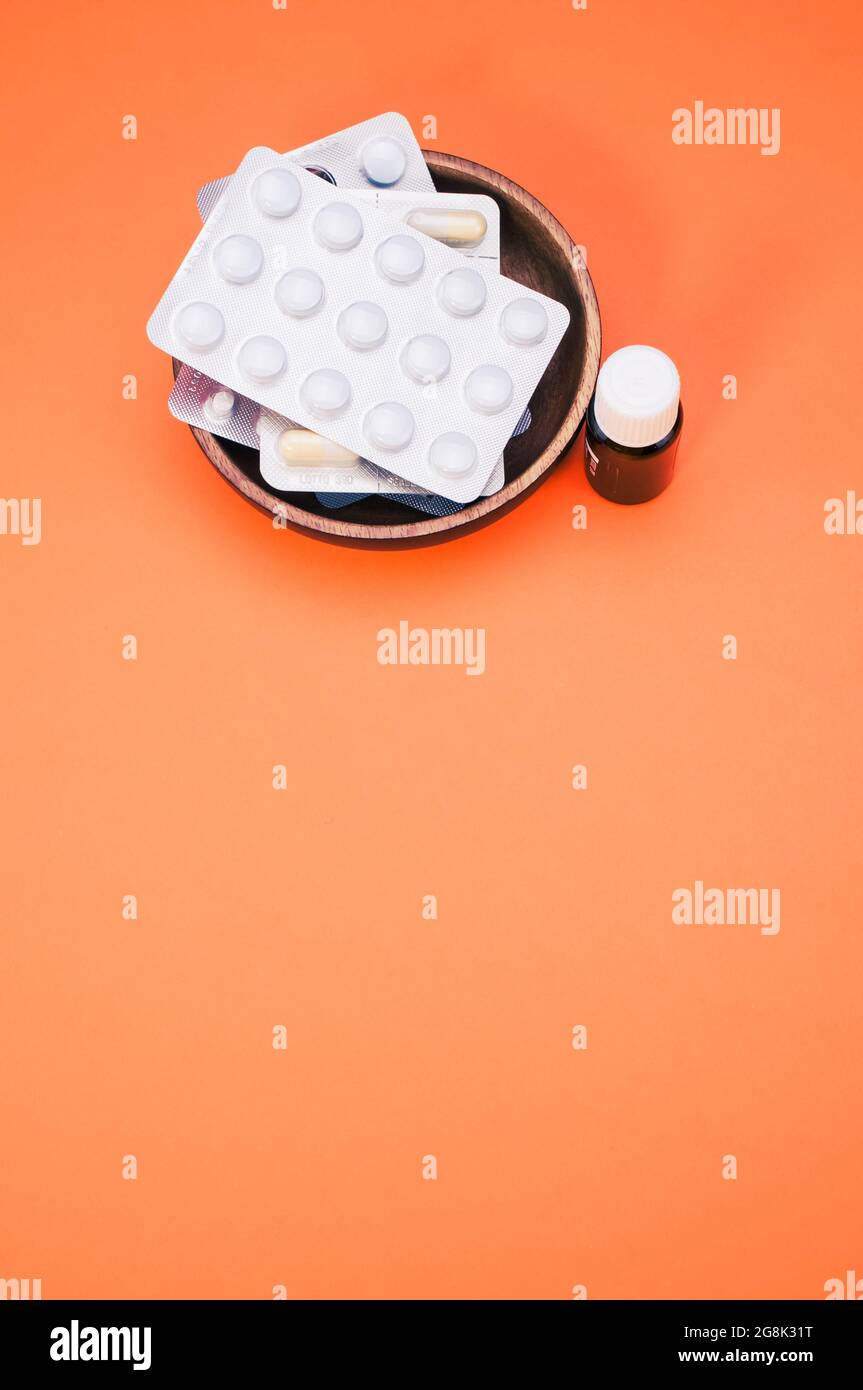 Small bowl full of pill blister packs and a vial isolated on an orange ...