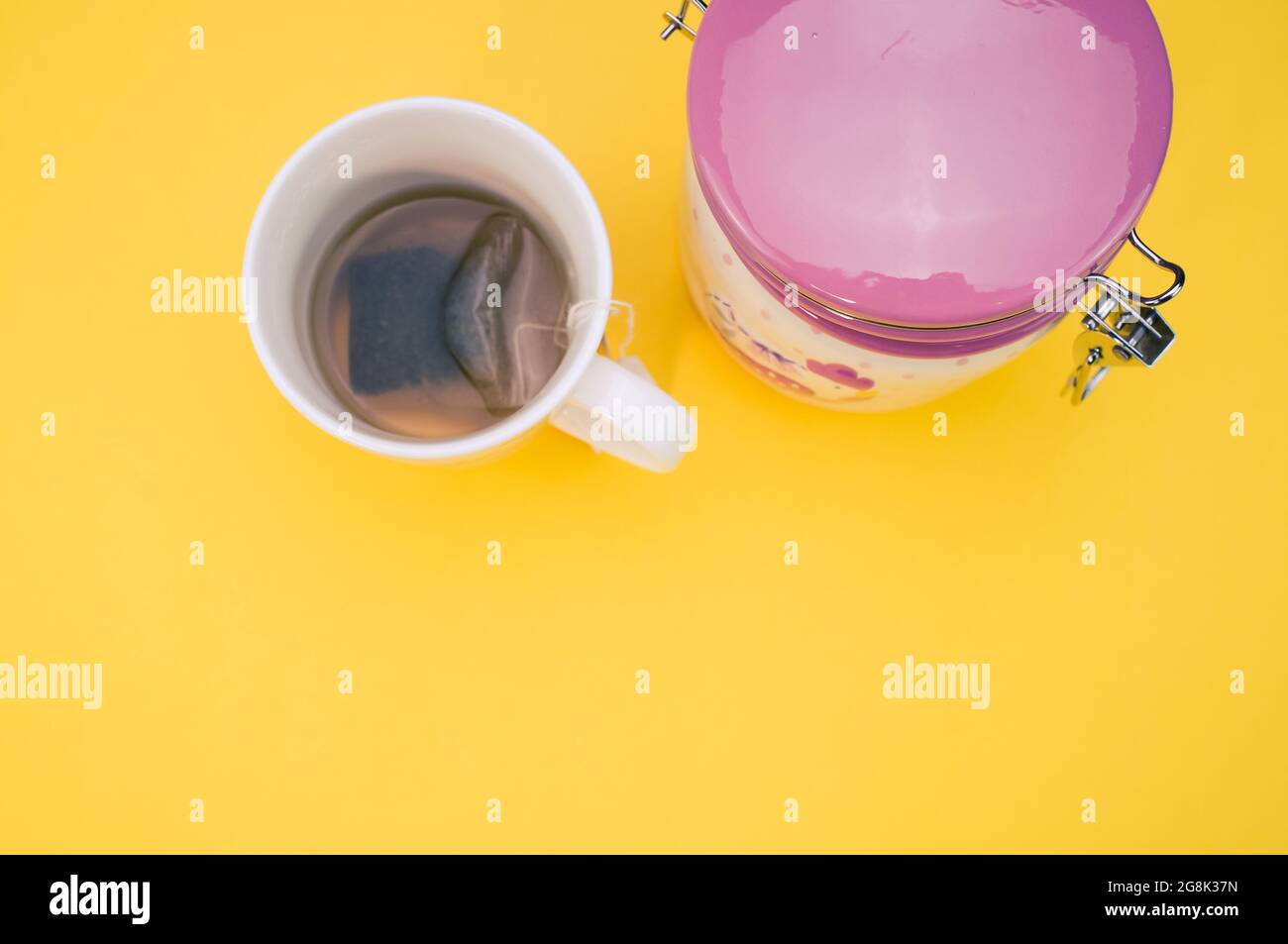 Plastic canister for tea and a cup of hot tea isolated on a yellow ...