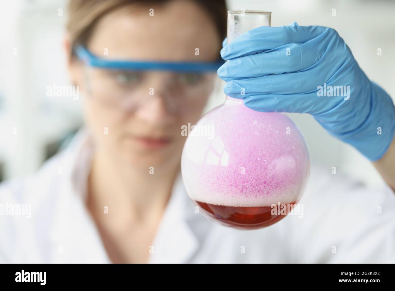 Woman scientist holding flask with purple liquid with foam in ...