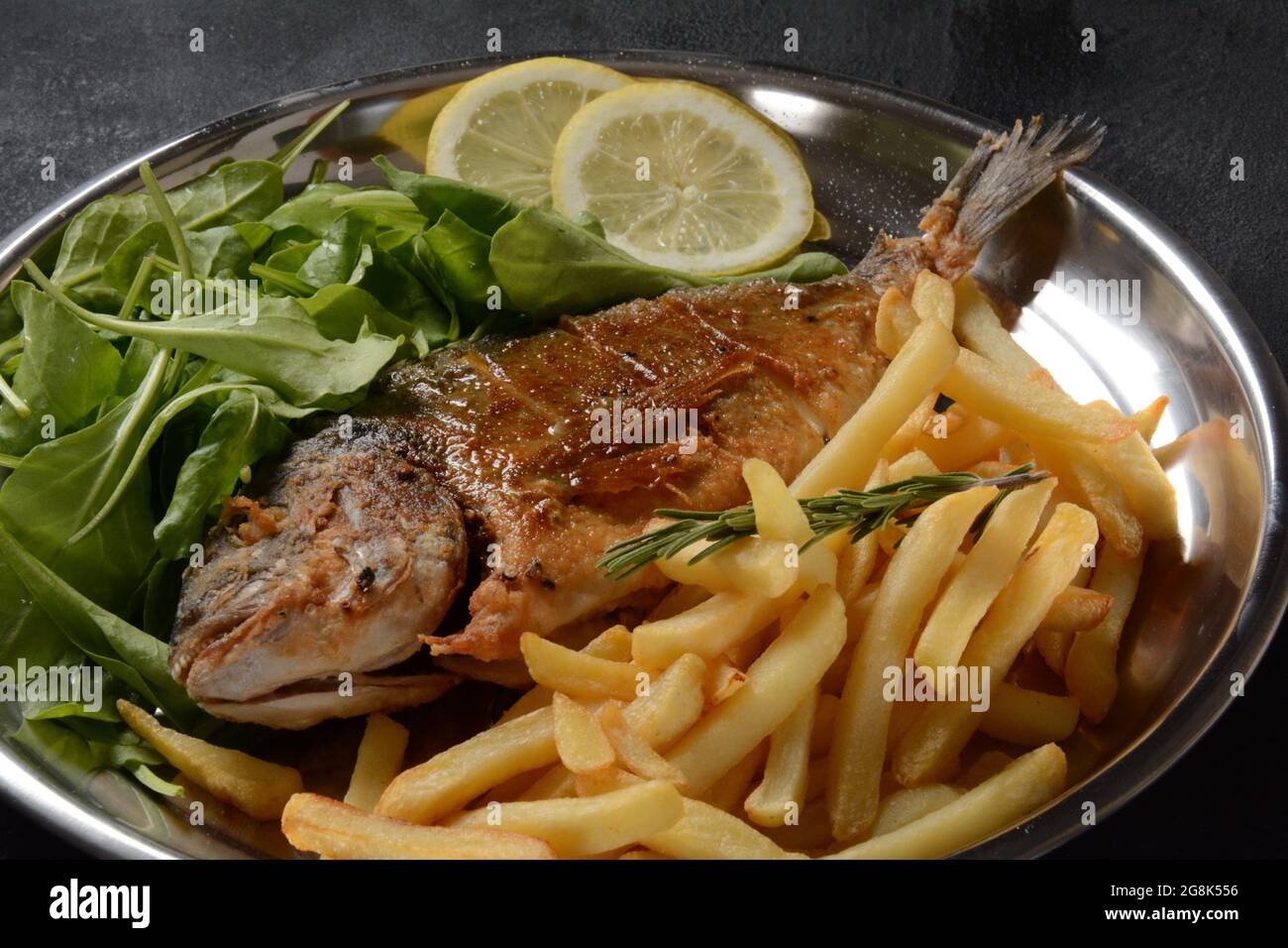 Fried fish dorado with potatoes chips, fresh herbs and lemon Stock ...