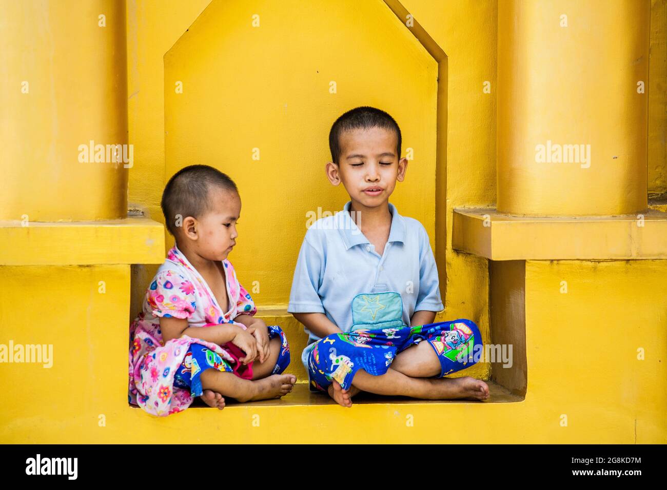 Young Burmese boy sits in lotus position meditating as younger sister ...