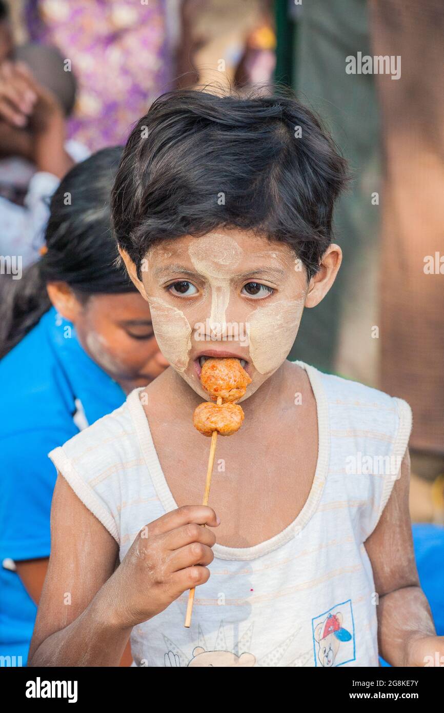 Cute young Burmese child with thanaka yellow paste face powder eating ...