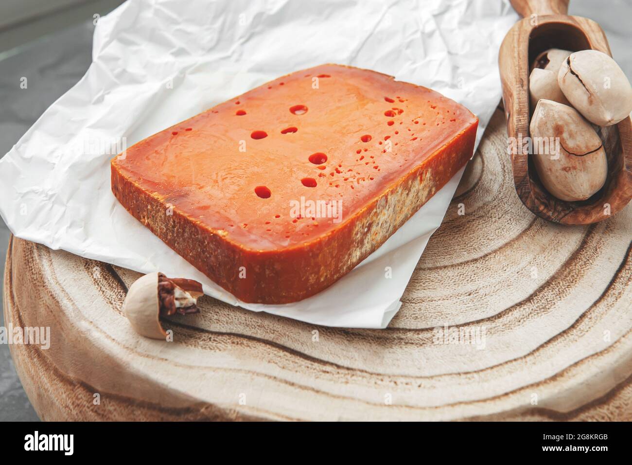 large piece of cheddar cheese with macadamia nuts on a wooden board. A ...