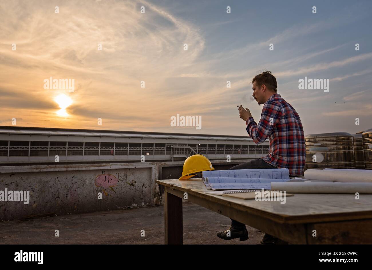 Engineer sitting alone and smoking on roof top after work at senset ...